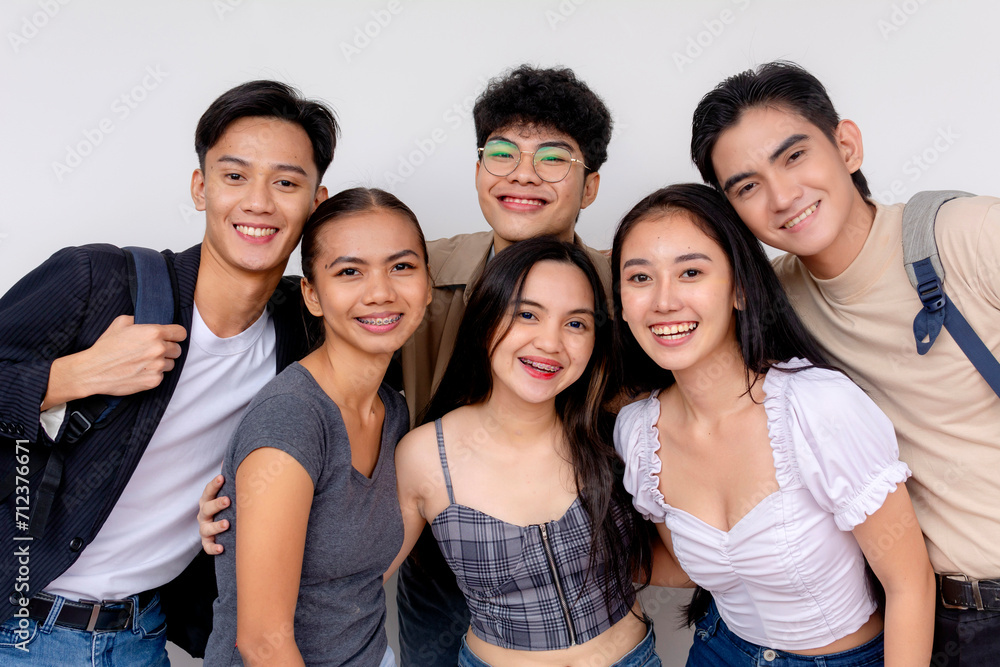 A diverse group of six happy young adults huddle together, smiling for ...