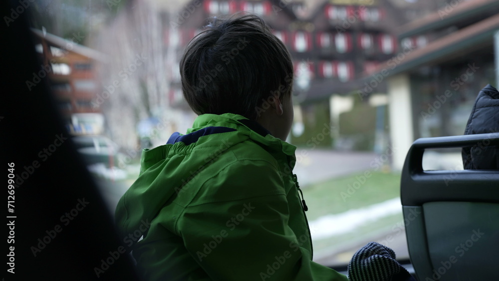 Child observing city from bus window seat wearing raincoat. Passenger ...
