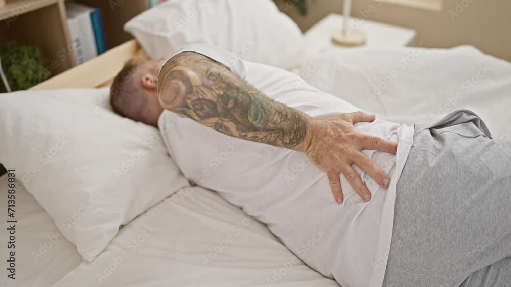 Handsome young man in pain, suffering from a back injury, lying in bed ...