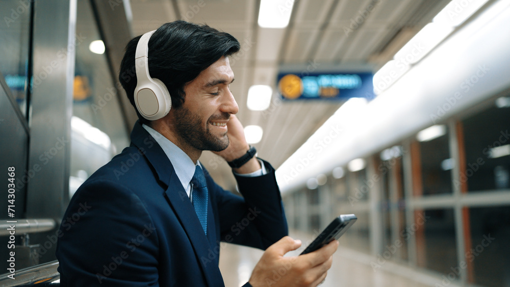Smart business man listening music by headphone while waiting train at ...
