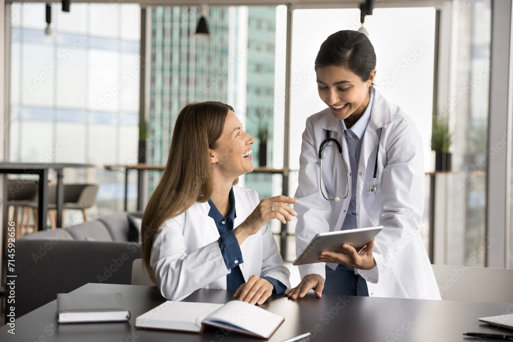 Two diverse female doctor colleagues using tablet at workplace table ...