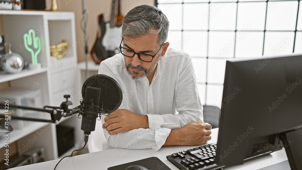 Grey-haired, young hispanic man on-air at radio studio, a serious news ...