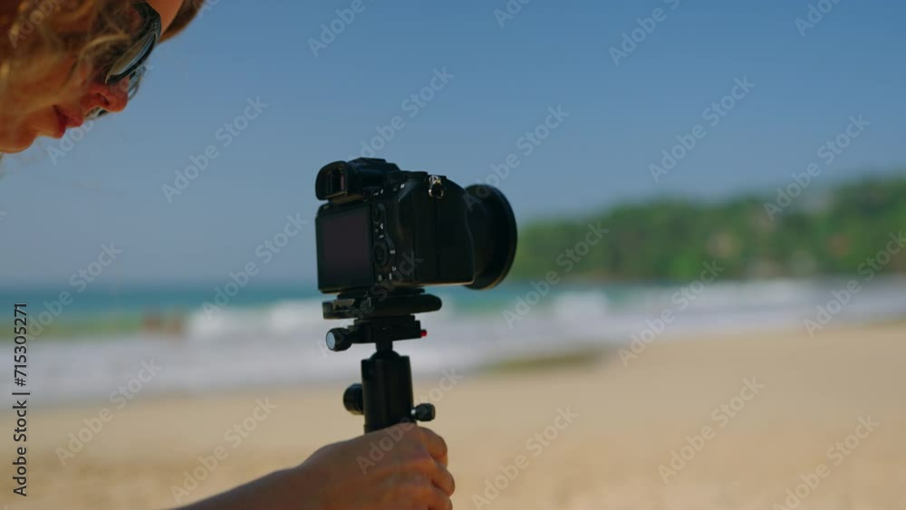 Female vlogger adjusts DSLR on tripod at sunny beach for content ...