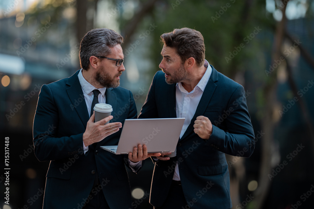 Excited business men team using laptop outdoor. Businessmen looking ...