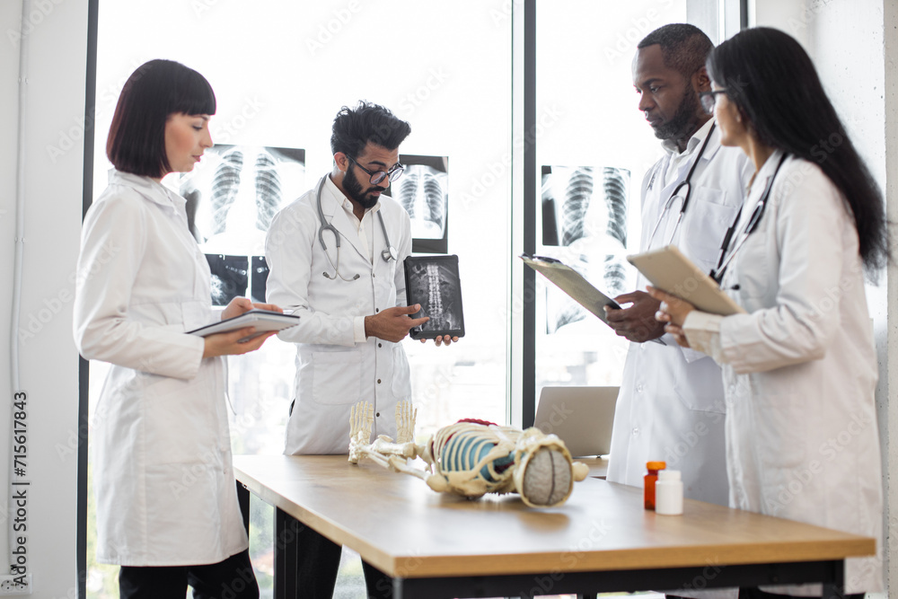 Young adult male teacher in class, holding x-ray of spine on tablet and ...