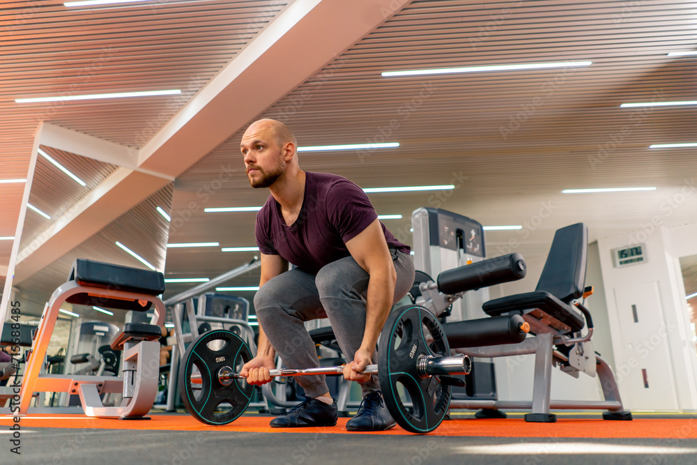 male bodybuilder doing strength exercises with a barbell in the gym ...