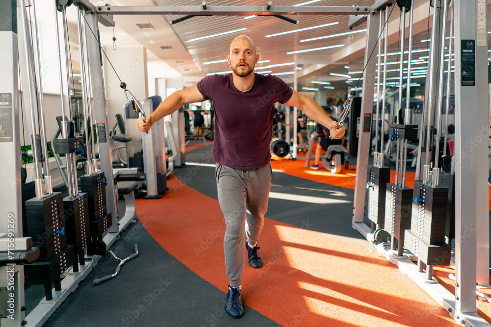 bald bodybuilder doing strength exercises on arms on exercise machine ...