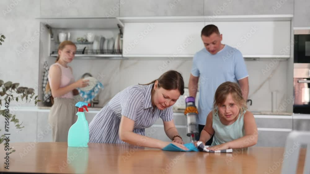Teenage daughter dusting the table while parents and youngest daughter ...