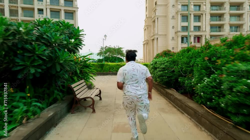 back view of a man running and in a lush garden pathway with benches ...