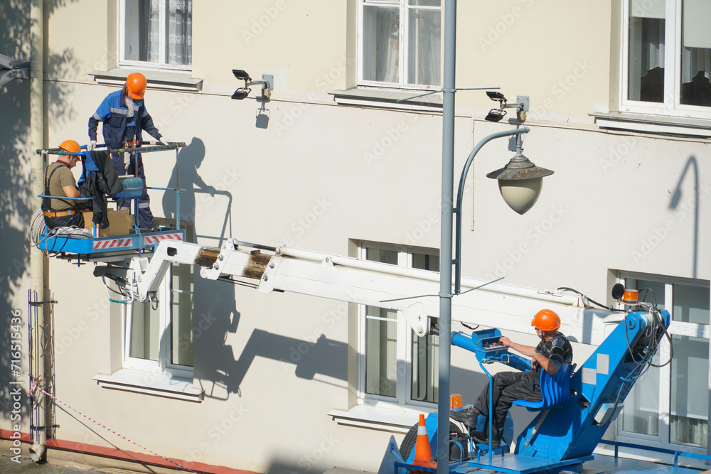 A worker in the bucket of a crane is installing lighting on the facade ...