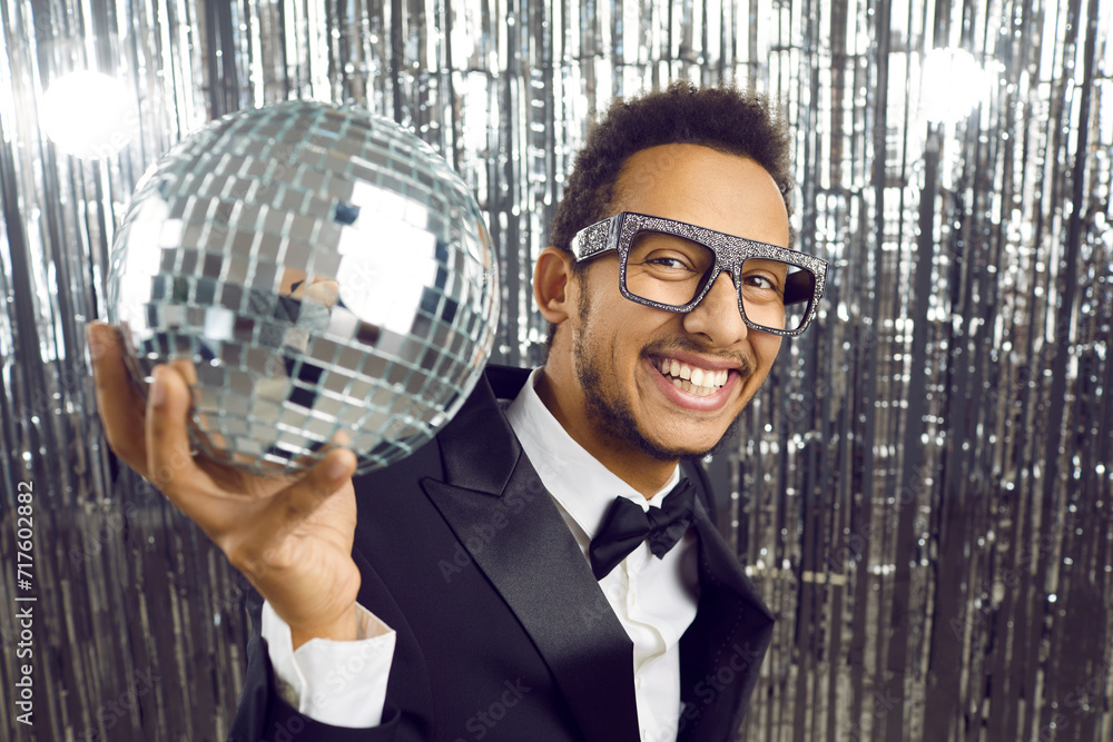 Portrait of overjoyed black man in suit and glitter glasses hold disco ...