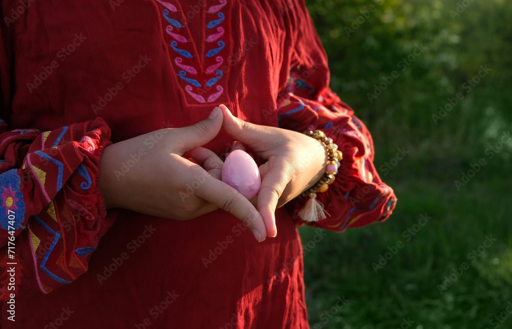 woman hands in Yoni mudra with rose quartz egg on red dress outdoor ...
