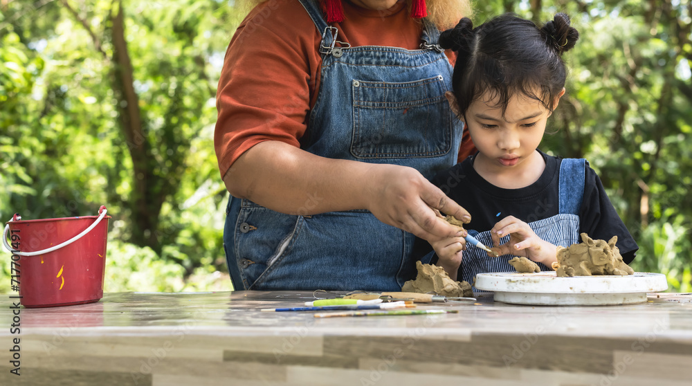 Mother teaching daughter how to make clay pottery in outdoors activity ...