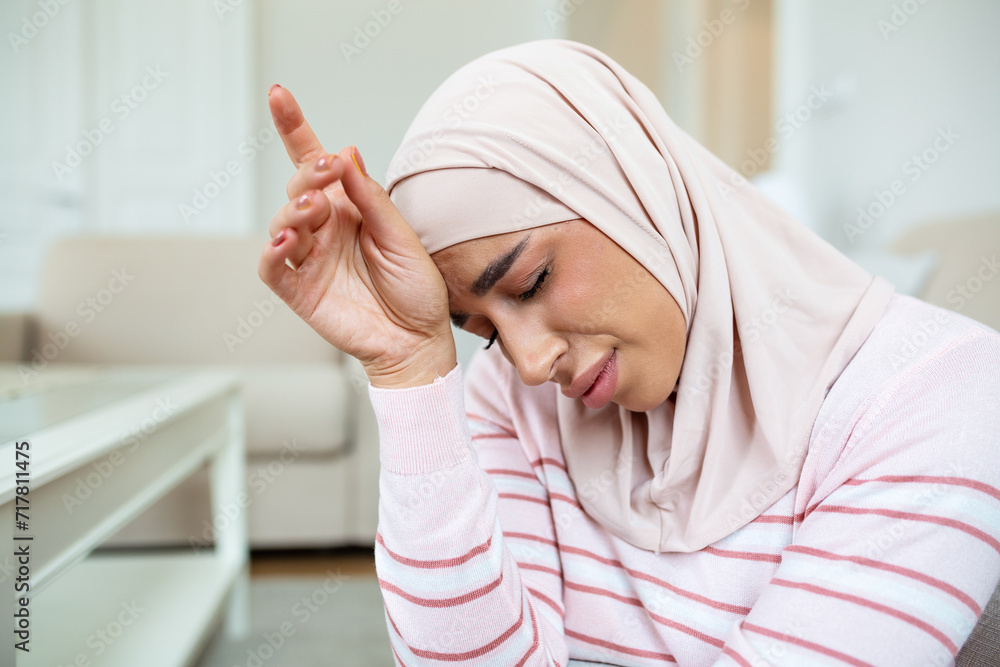 Portrait of a young Arabic Muslim woman sitting on the couch at home ...