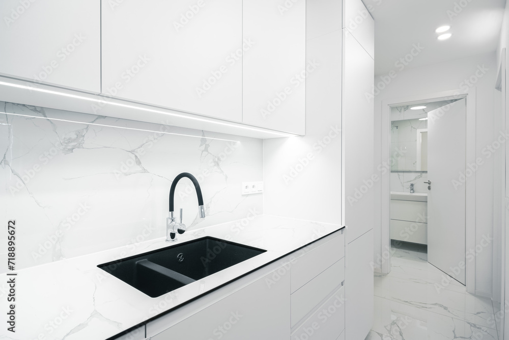 A Modern kitchen with white cabinets, marble countertops, a black sink ...