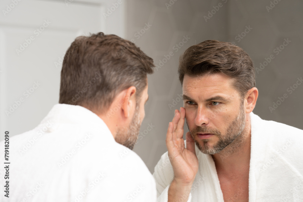 a man in a white bathrobe in the bathroom looking at the skin on his ...