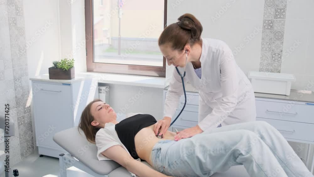 A female doctor with a stethoscope examines the abdomen of a young ...