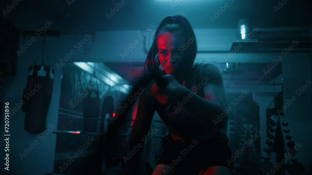Athletic woman trains with battle ropes in dim boxing gym with LED ...