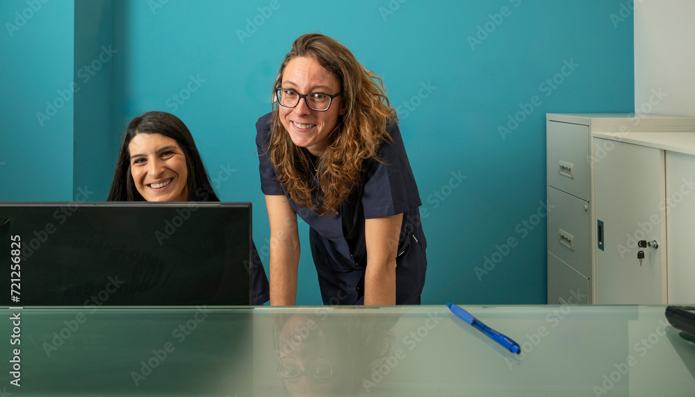 Two women share a light-hearted moment behind an office reception desk ...