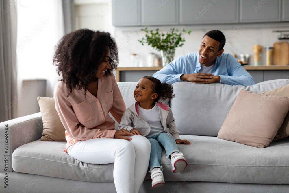 Happy black parents resting with cute little daughter, sitting on sofa ...