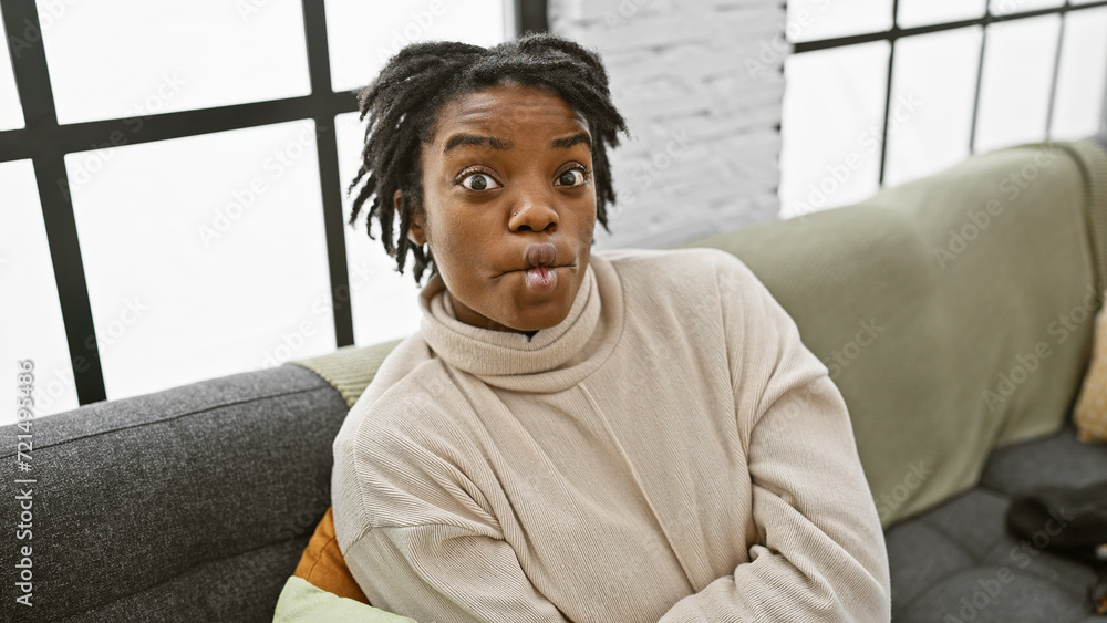 Woman with dreadlocks making a playful face while relaxing on a sofa in ...