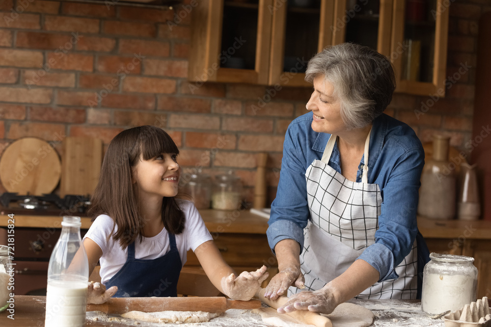 Foto de Granny teaches to cook. Smiling preteen hispanic girl in apron ...