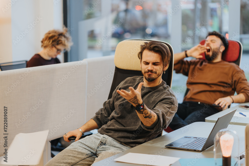 Two tired male colleagues in a modern office setup stretch and yawn ...