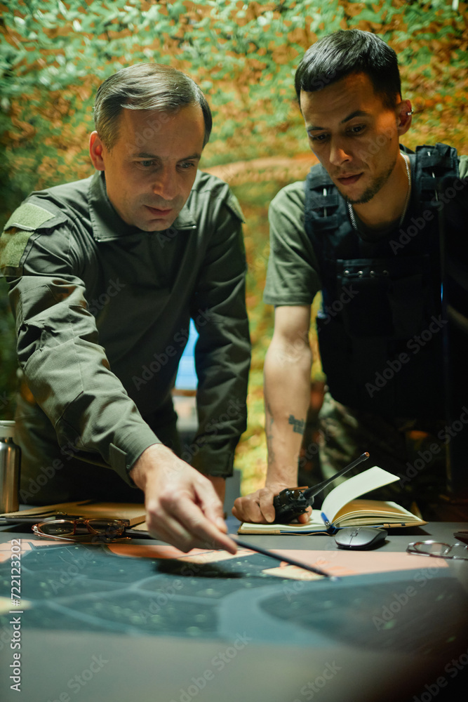 Young and mature officers in uniform looking at map while one of them ...
