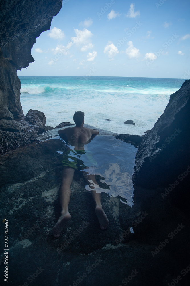 Person sitting on rocks inside a cave looking out at the ocean Stock ...