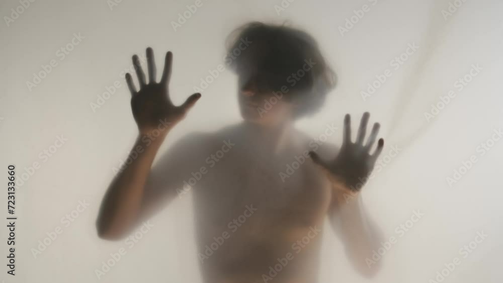 A blurred silhouette of a man with a bare torso behind a frosted curtain or glass. A man touches ...