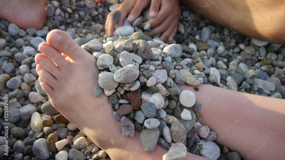 Close-up of woman's feet on a pebble beach, Hands placing pebbles over ...