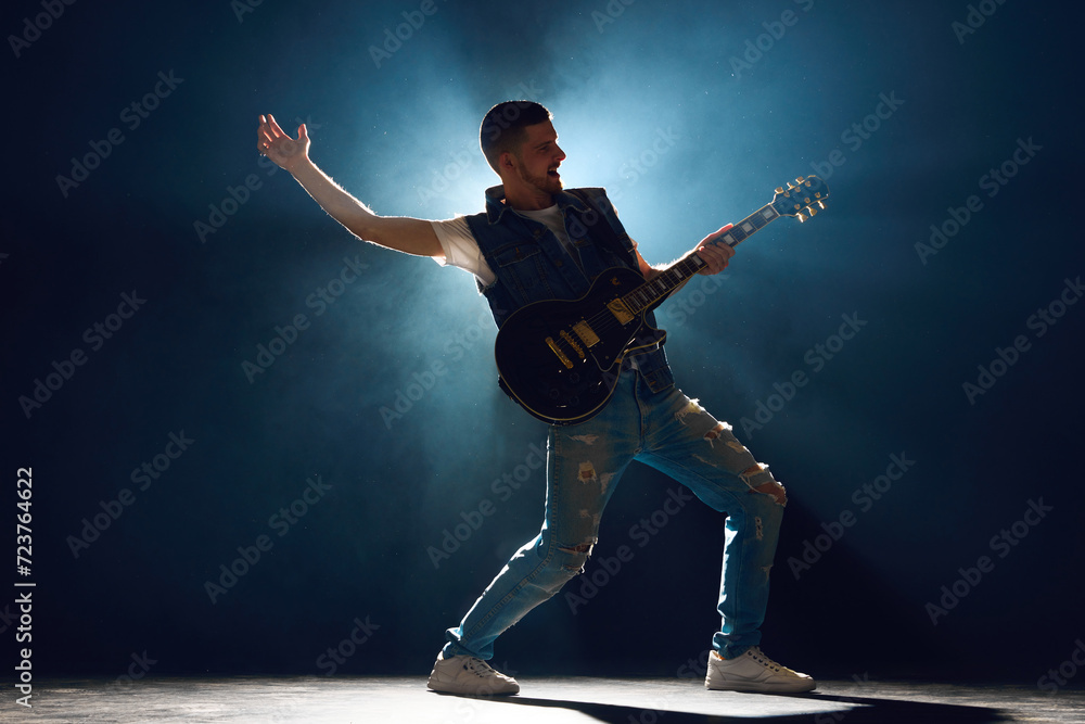 Full length portrait of music artist in ripped jeans and vest bending ...