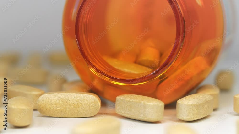 Big yellow tablets lies on table. Opened orange jar with vitamins ...