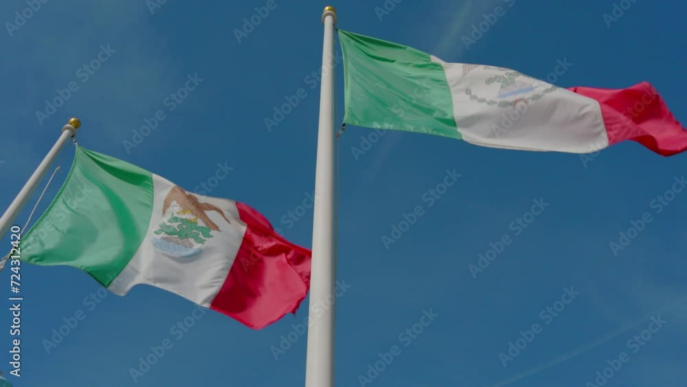 Two Mexican flags flutter in the wind atop poles, vibrant green, white ...