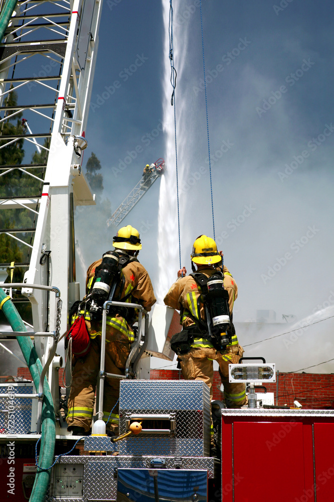 Vertical image of Firefighters standing on a hook and ladder fire ...