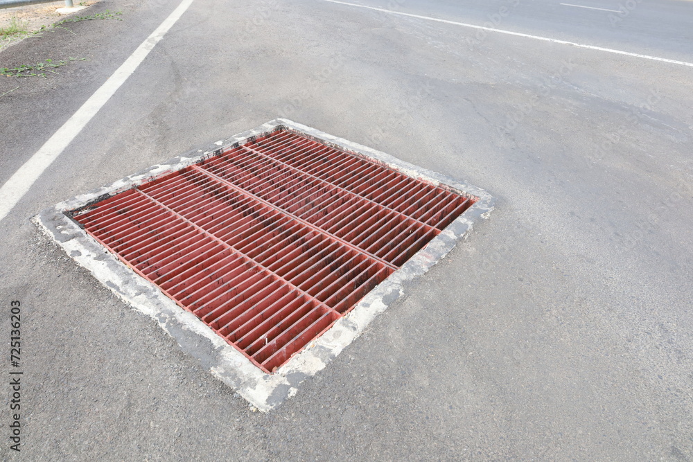 Drainage grates on paved roads. Red metal grating covers a sewer pipe ...