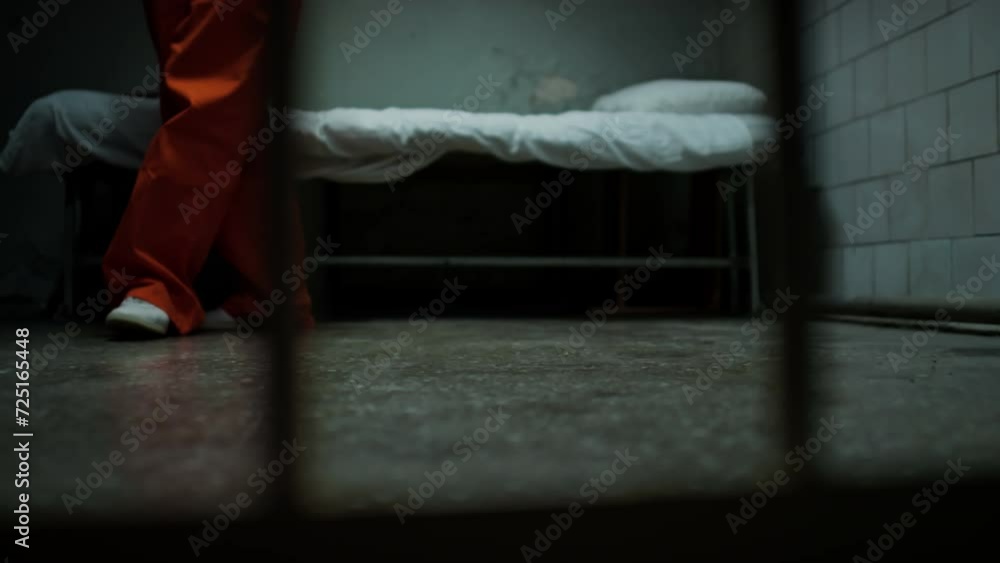 Low section shot through bars of legs of anxious inmate in orange jail ...
