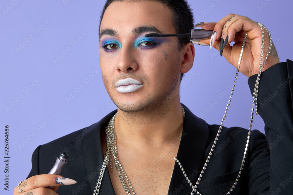 transvestite man applying ink on eyelashes, isolated over purple ...