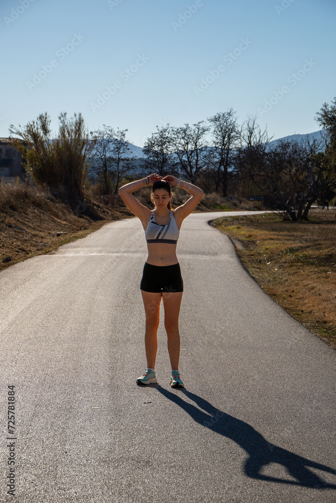 Beautiful young slim runner, dressed in tight sportswear, tying a bun ...