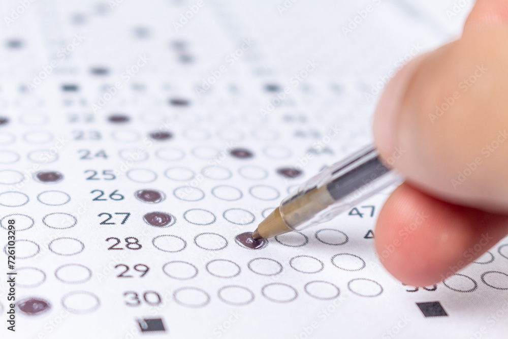 Hand filling out an exam answer sheet with a pen, concept for public ...