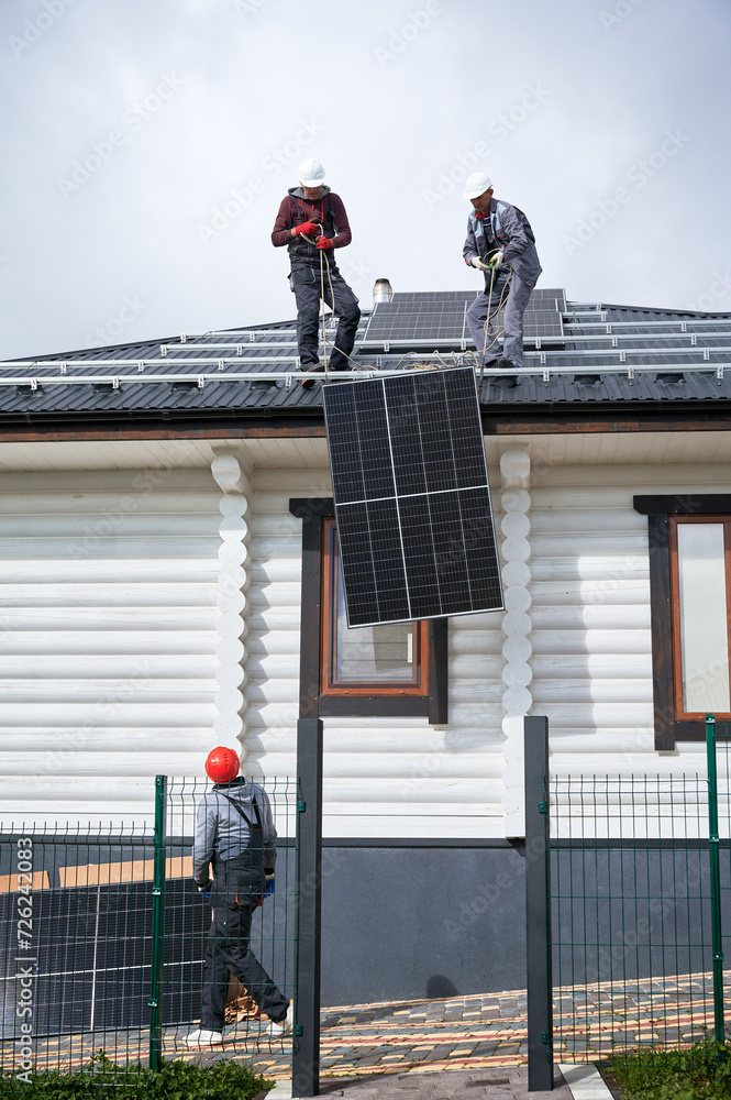 Men workers installing solar panel system on roof of house ...
