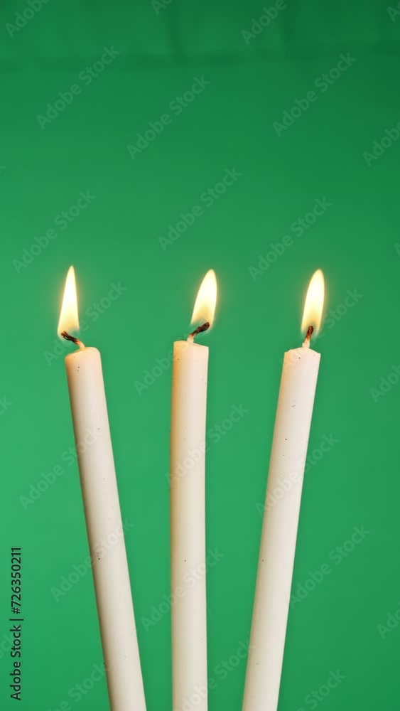 Vertical three candles are lit on a green background. Candle flames on ...
