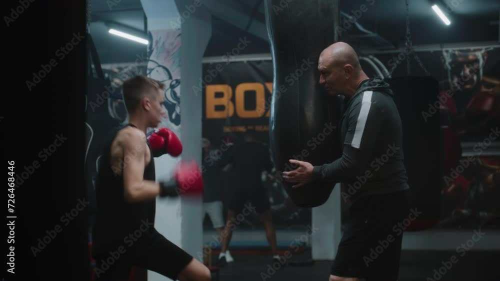 Young boxer in boxing gloves exercises with trainer in dark gym before ...