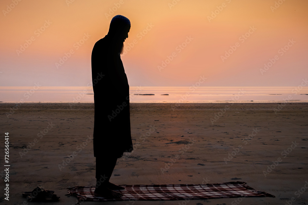 Asian Muslim man praying under the open sky by the sea at sunset ...