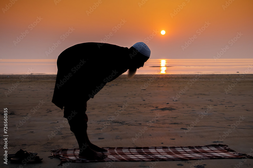 Asian Muslim man praying under the open sky by the sea at sunset ...