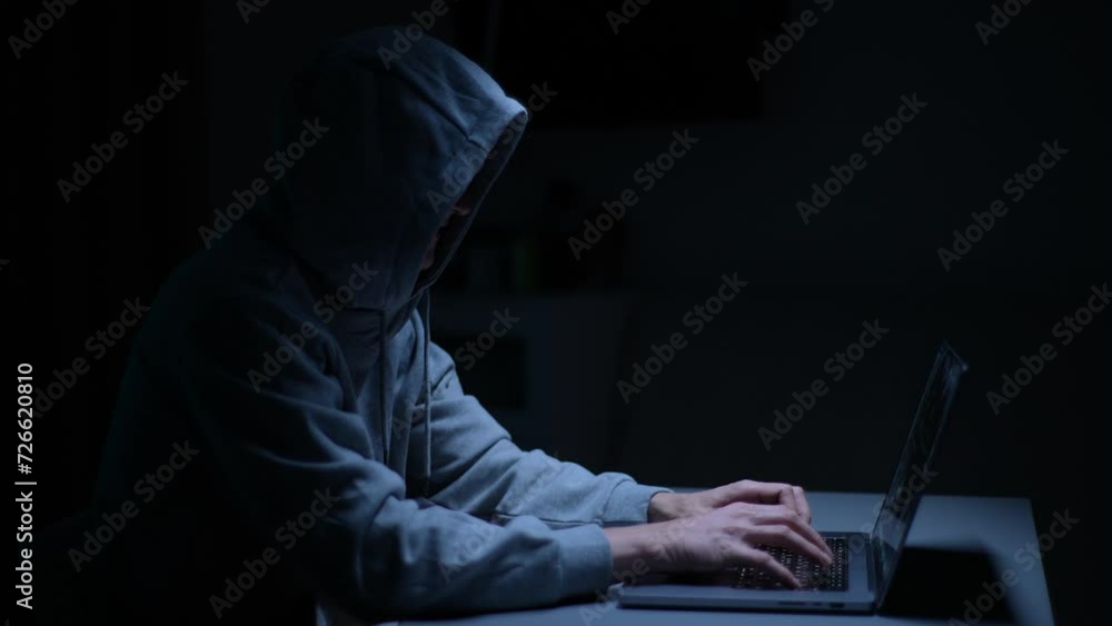 Dangerous hacker male wearing sweatshirt breaking computer system and typing password for ...