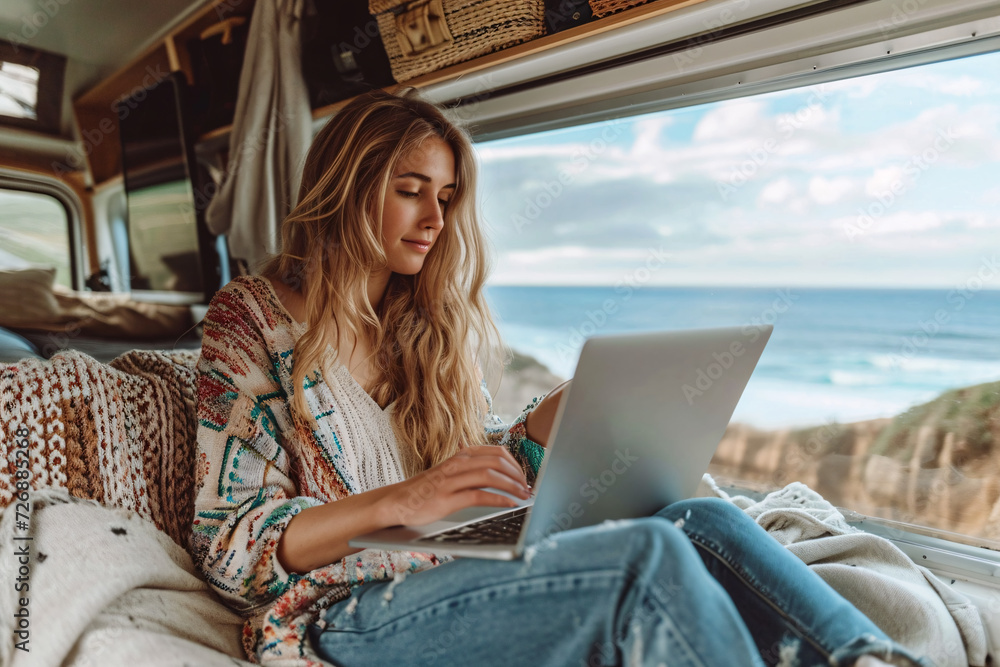 Woman working on laptop inside a cozy camper van with a scenic ocean ...