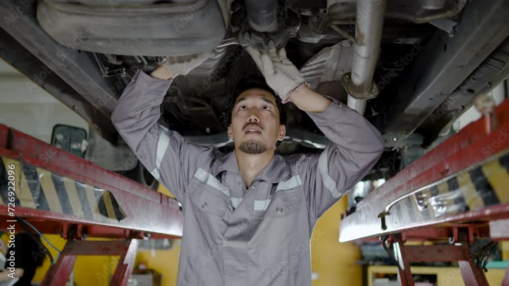 Young asian mechanic working underneath car lifting machine at the ...