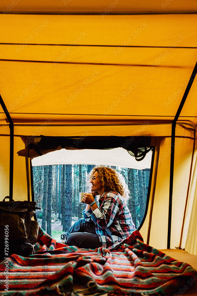 Happy lonely adult caucasian woman sit down outside a tent enjoying a ...