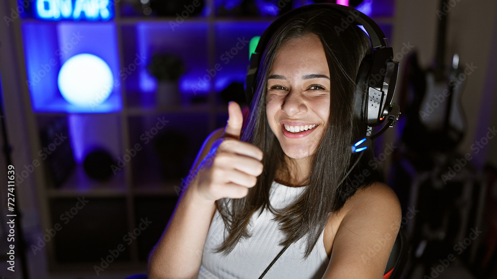 Young, beautiful hispanic woman streamer confidently gives a thumb-up ...